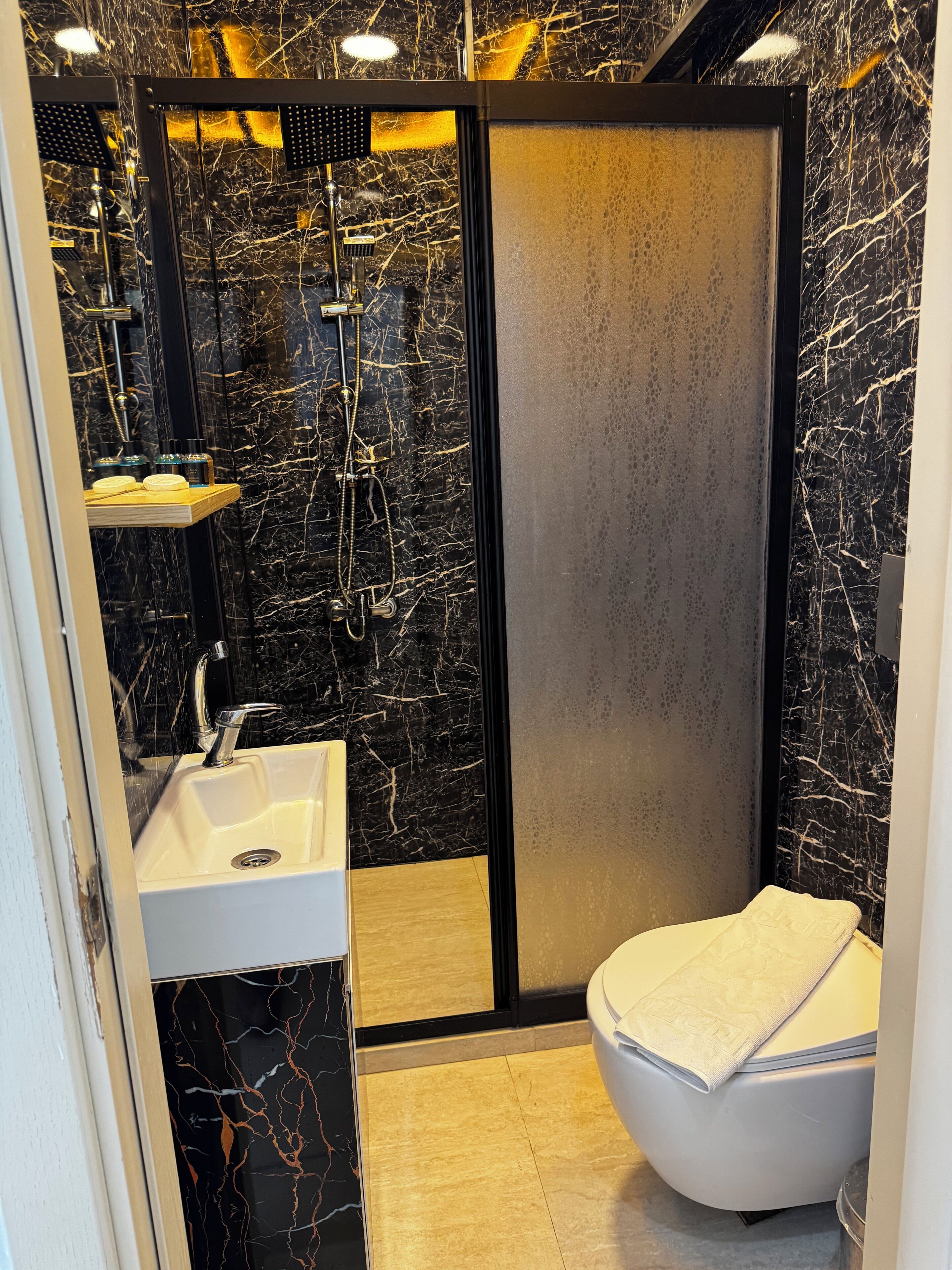 Um banheiro moderno com pia de mármore, vaso sanitário separado e chuveiro com porta de vidro.