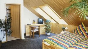 Um quarto de sótão aconchegante com teto inclinado, uma escrivaninha de madeira, uma cadeira, uma cama com roupa de cama colorida e várias plantas em vasos.