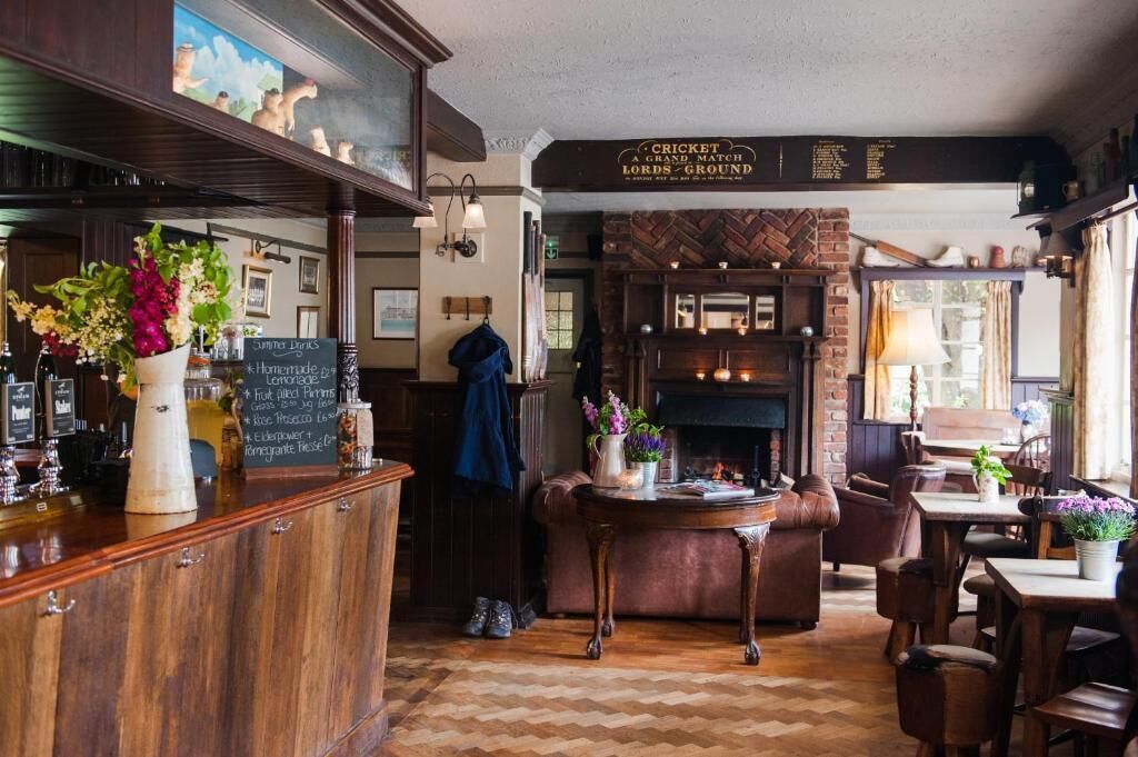 Um pub com área de bar, assentos, lareira e uma placa sobre o esporte críquete.