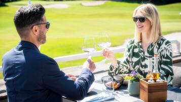 Um casal brindando com taças de vinho em uma mesa com vista para um campo de golfe.