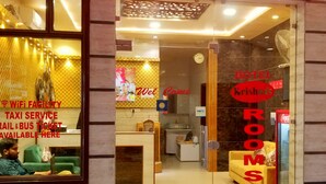Entrada do Hotel Krishna's, com balcão de recepção, um relógio e um refrigerador de Coca-Cola.