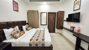 Quarto de hotel com cama, televisão, escrivaninha e guarda-roupa.