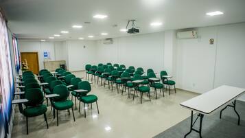 Uma sala de conferência com fileiras de cadeiras e mesas verdes, um projetor e um aparelho de ar condicionado na parede.