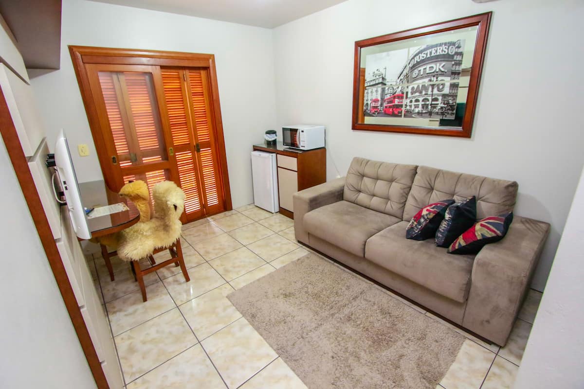 Uma sala de estar com sofá, uma mesinha, uma cadeira, uma televisão e um frigorífico.