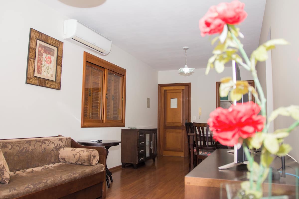 Uma sala de estar com sofá, mesa de jantar, armário de madeira e porta para outro cômodo.