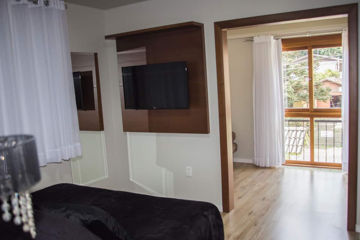 Quarto com cama, televisão na parede e porta de vidro deslizante para uma varanda.