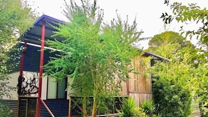 Uma casa de madeira tradicional com escadaria de madeira que leva a um alpendre, cercada por vegetação exuberante.