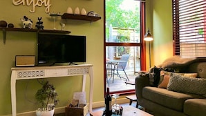 Uma sala de estar aconchegante com televisão, uma mesinha de console branca, uma planta em vaso e um sofá com almofadas.