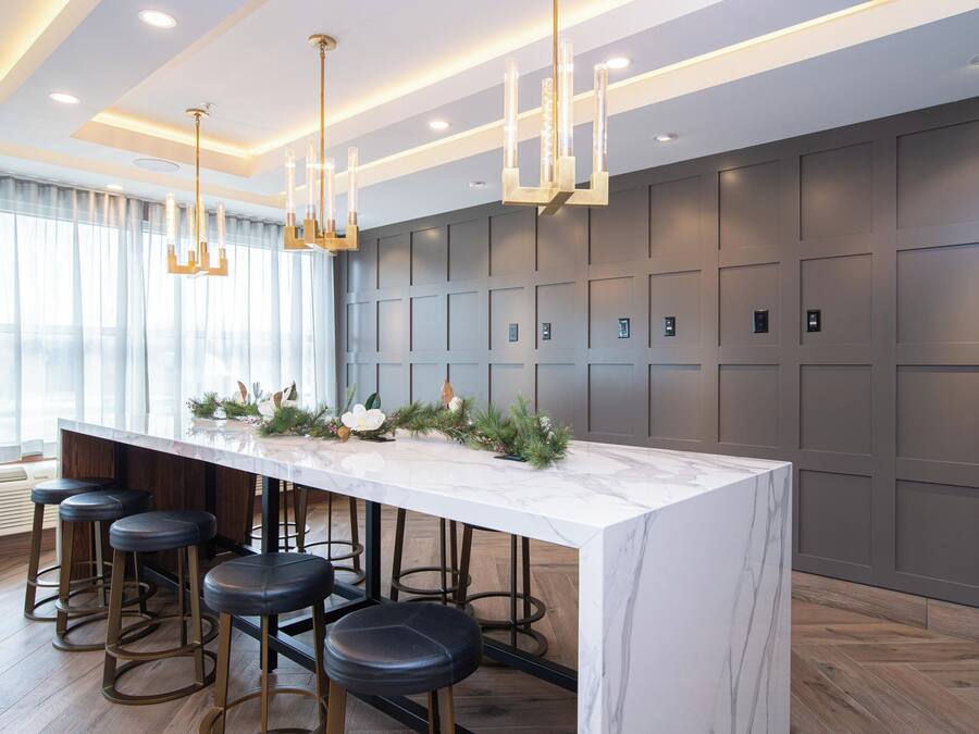 Uma cozinha moderna com bancada de mármore, banquetas de bar, iluminação pendente e um arranjo decorativo de plantas.
