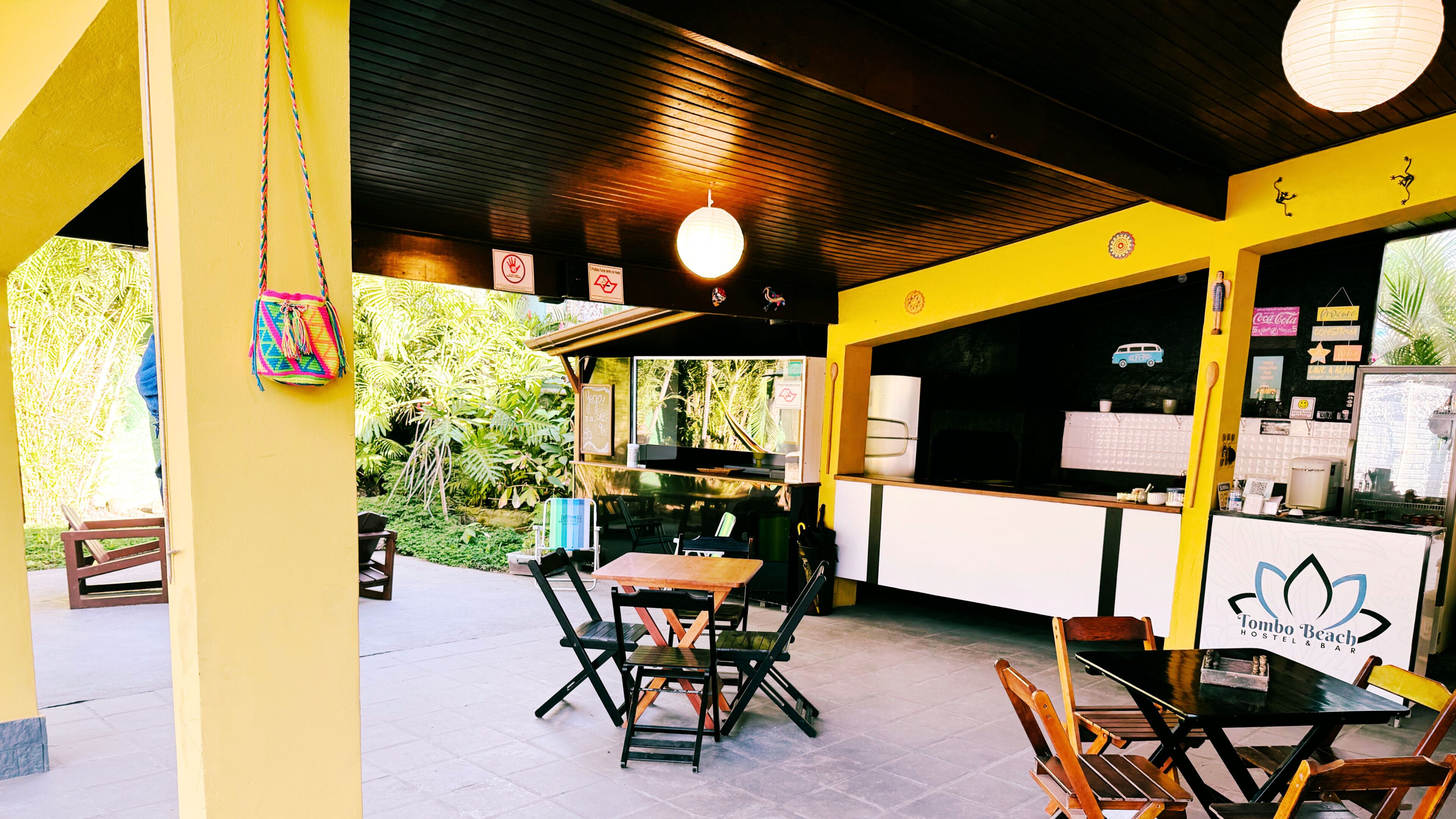 Uma área externa com mesas e cadeiras, um balcão com uma placa e vista para o verde.