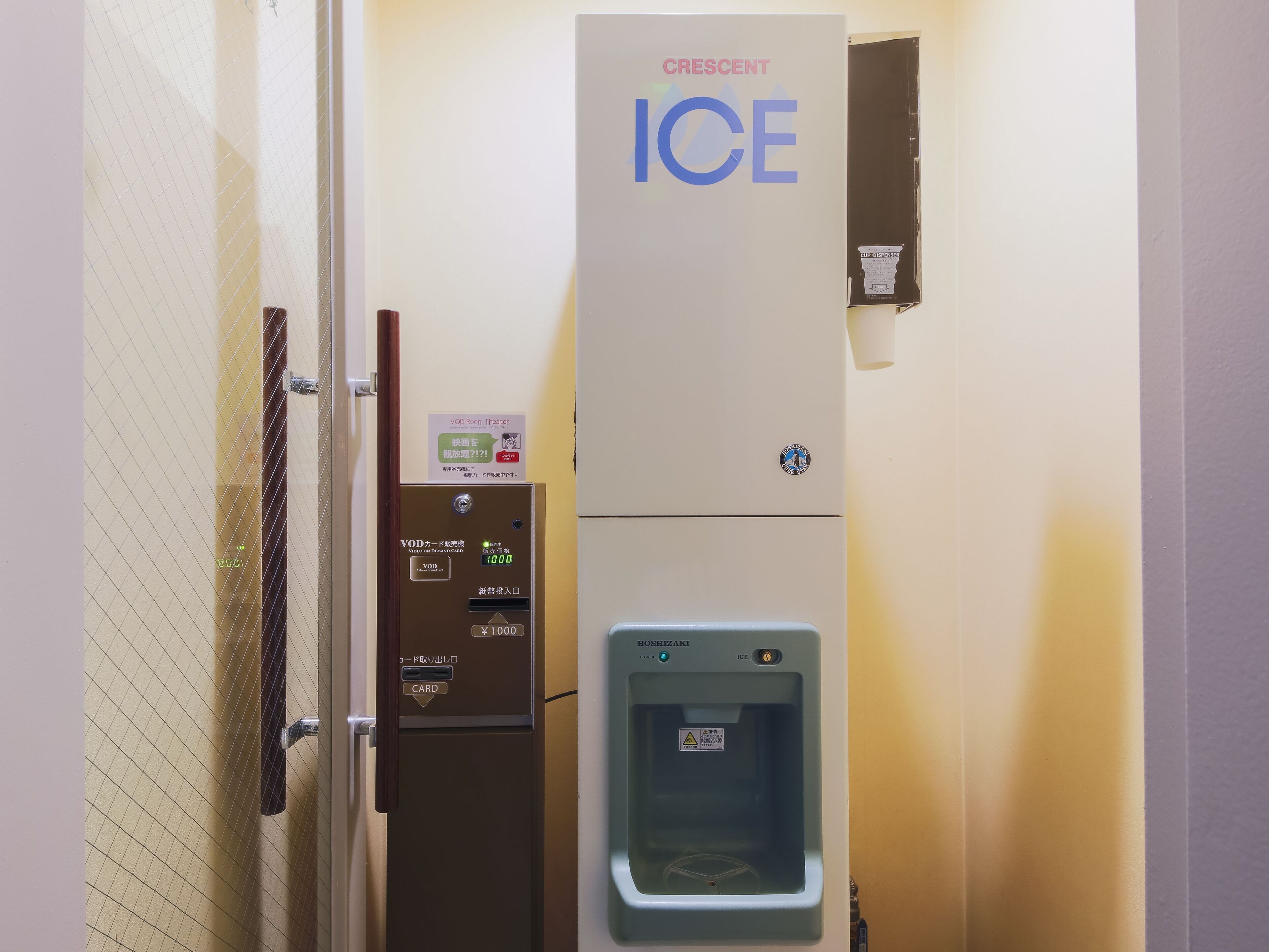 Máquina de vendas com dispensador de bebidas, leitor de cartão e placa indicando sala de cinema VOD.