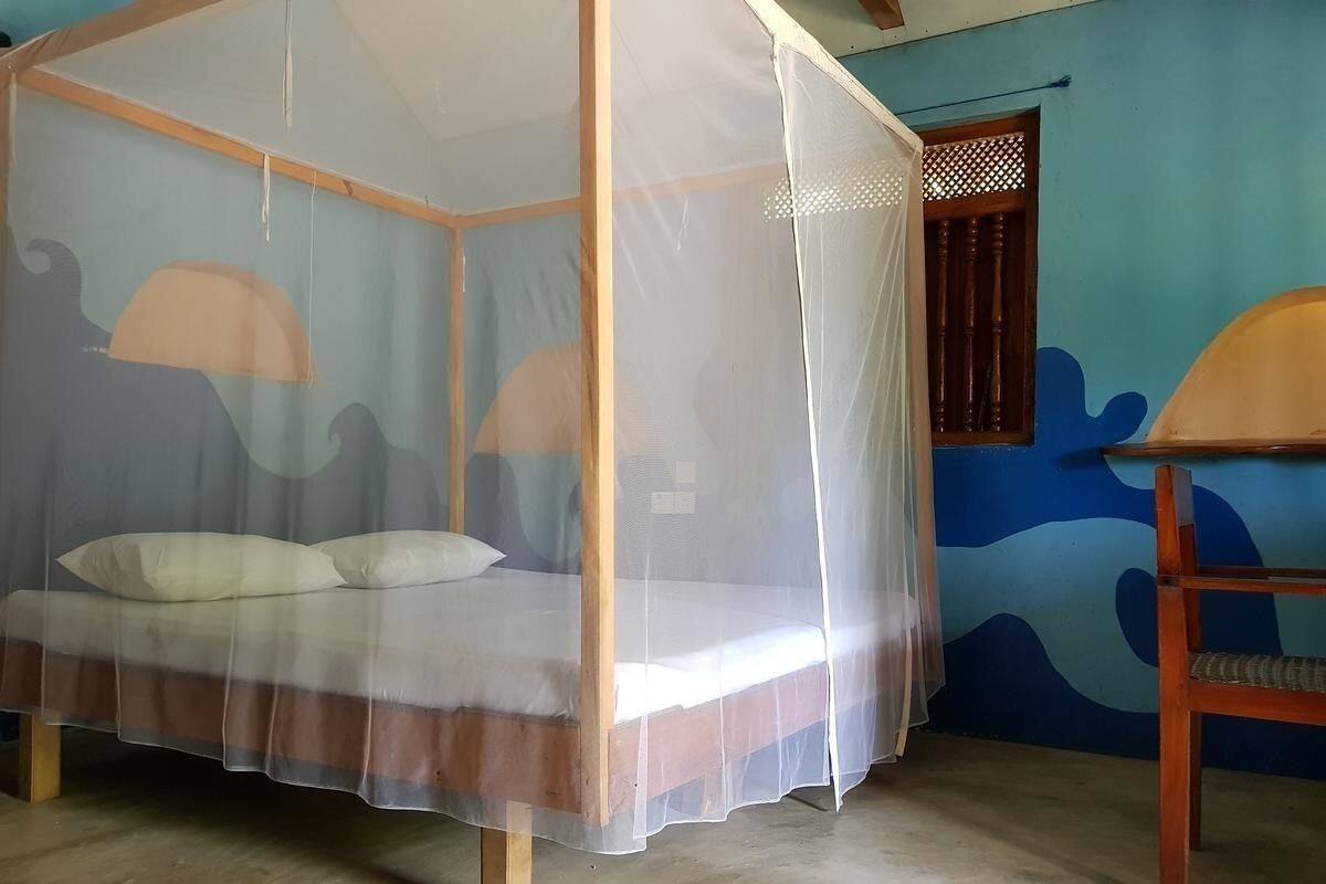 Quarto com uma cama de dossel, uma cadeira de madeira e uma parede azul com padrão de ondas.