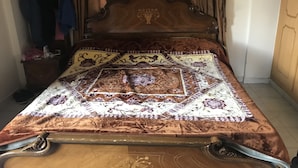 Uma cama com colcha estampada, cabeceira de madeira e estrutura de metal.