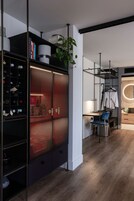 Quarto moderno com piso de madeira, estante preta com diversos objetos, uma cadeira azul e um roupão pendurado.