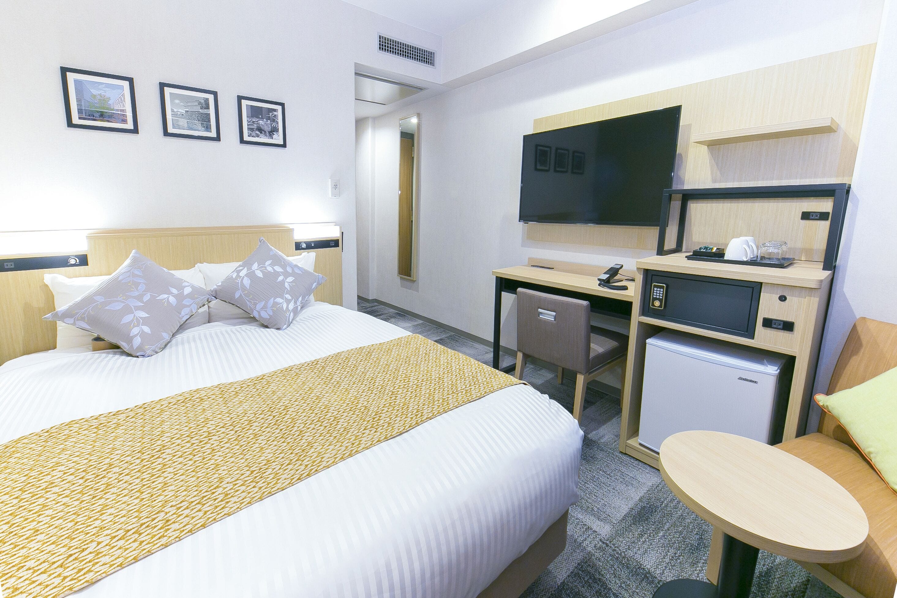 Quarto de hotel com cama, escrivaninha com computador, micro-ondas e pequena geladeira.