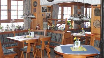 Um restaurante acolhedor com mobiliário de madeira, incluindo cabines e mesas, além de diversas decorações e plantas.