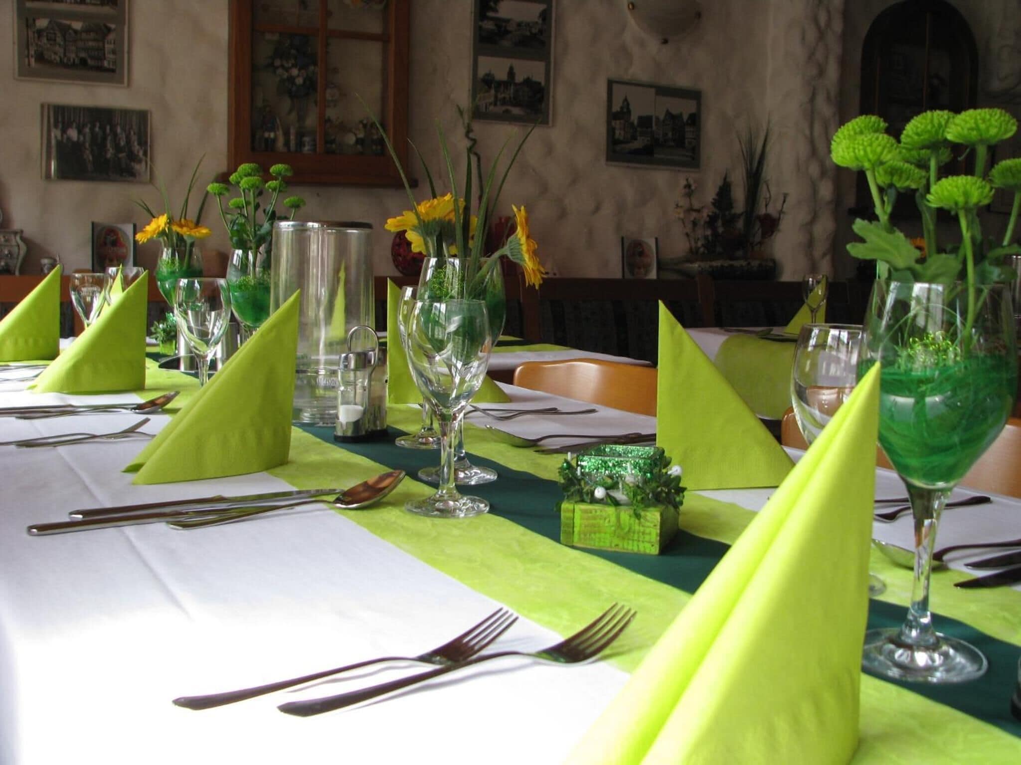 Uma mesa de jantar posta com guardanapos verdes, copos transparentes e talheres.
