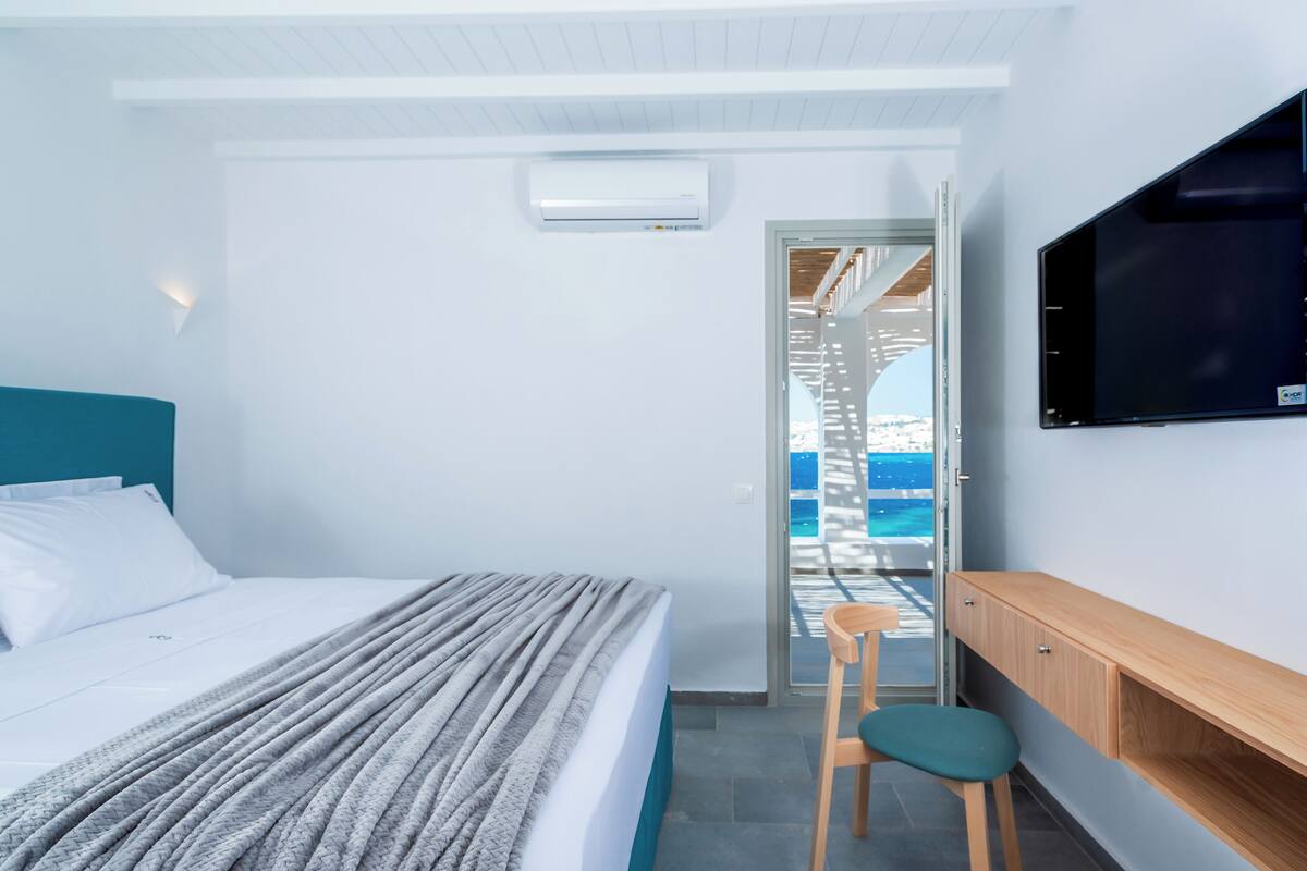 Quarto com cama, televisão presa na parede, escrivaninha e cadeira.