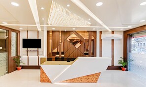Uma área de recepção moderna com uma televisão grande, uma luminária pendente decorativa e uma escadaria para os andares superiores.