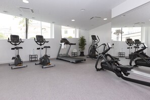 Academia com diversos equipamentos de cardio, esteira e um vaso de planta.