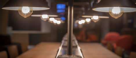 Várias luminárias pendentes com lâmpadas aparentes sobre uma mesa comprida em um ambiente com pouca luz.