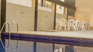 Um edifício moderno com área de piscina no terraço, incluindo piscina e cadeiras de plástico brancas.