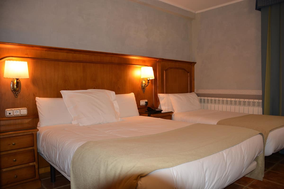 Quarto de hotel com duas camas, cabeceira de madeira, luminárias laterais e mesa de cabeceira com telefone.