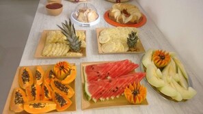 Uma mesa com diversos espetos de frutas, incluindo papaia, melancia e fatias de abacaxi, dispostos sobre um pano de mesa branco.