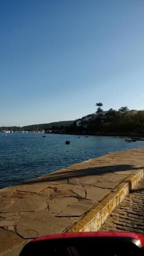 Vista costeira com calçada pavimentada, barcos na água e edifícios ao fundo.