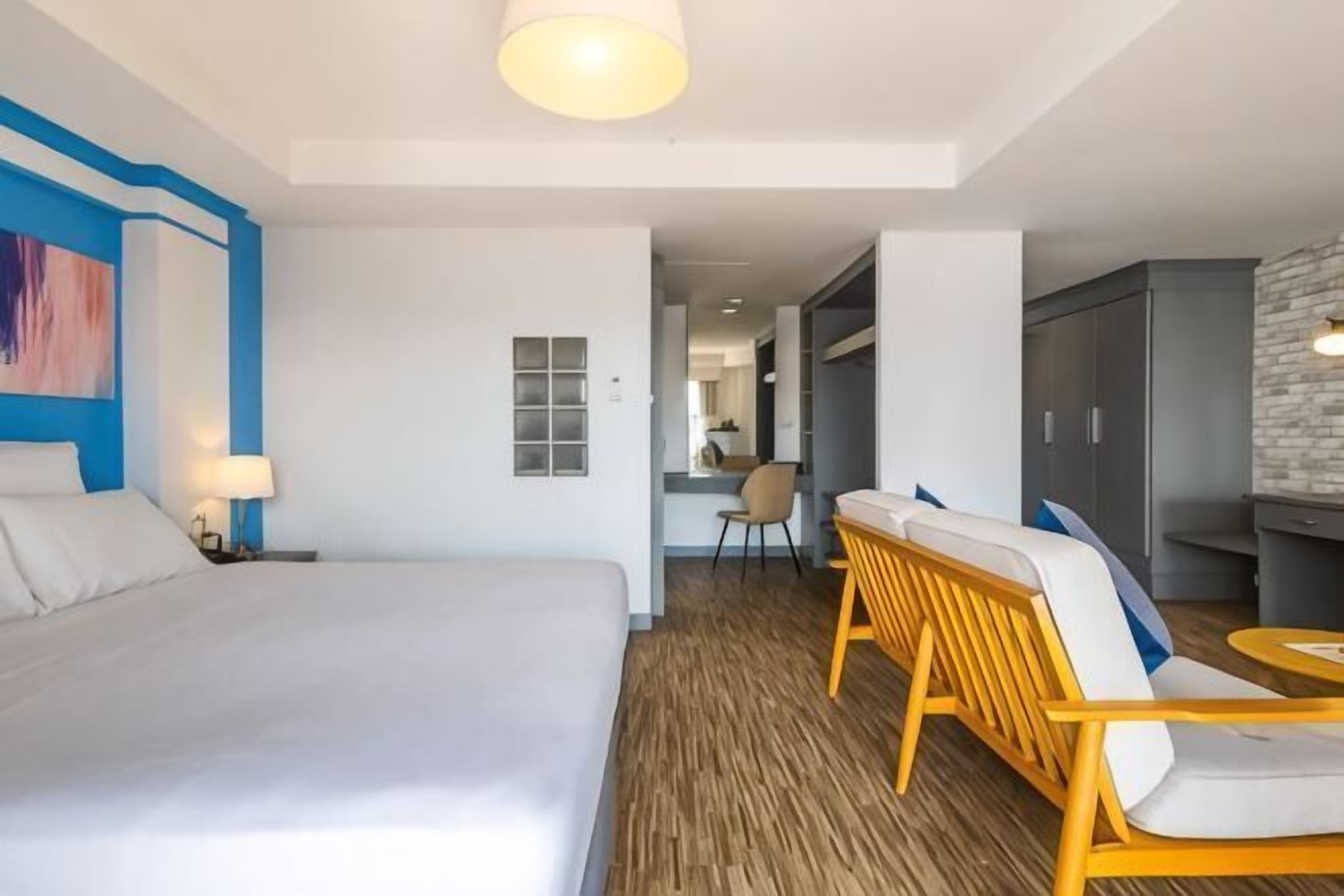 Quarto de hotel com cama, área de estar, cozinha compacta e banheiro visível através de uma porta aberta.