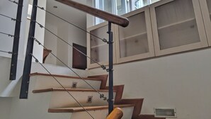 Uma escadaria com degraus de madeira e corrimãos de metal, que leva a um patamar onde está fixado um extintor de incêndio na parede.