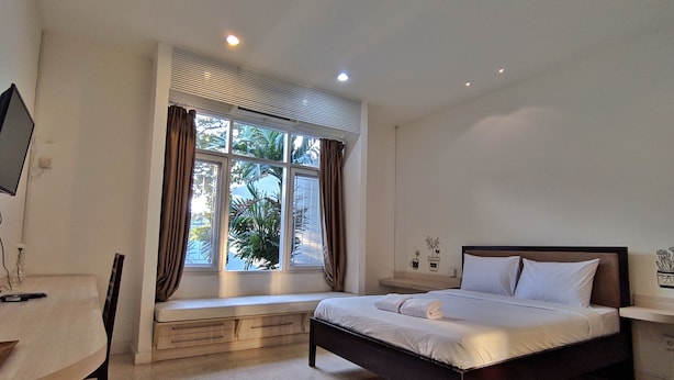 Quarto com cama, escrivaninha e janela com cortinas.