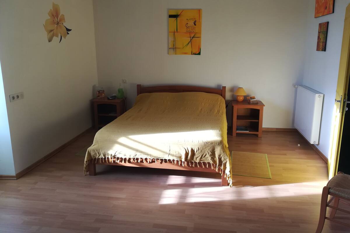 Quarto com cama de madeira, duas mesas de cabeceira, um radiador e uma cadeira.