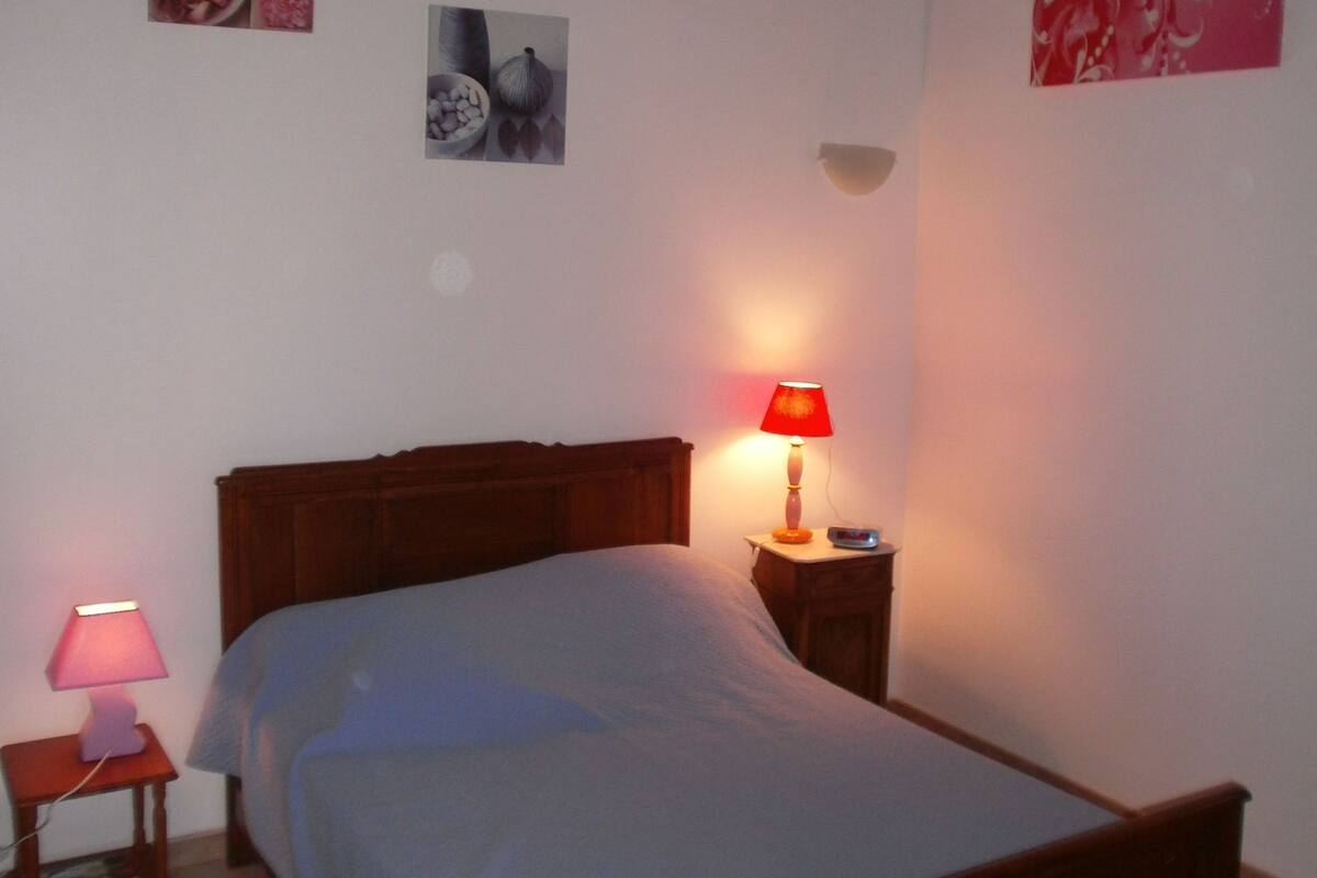 Quarto com cama, mesa de cabeceira com luminária, pequena mesa com luminária e decoração nas paredes.