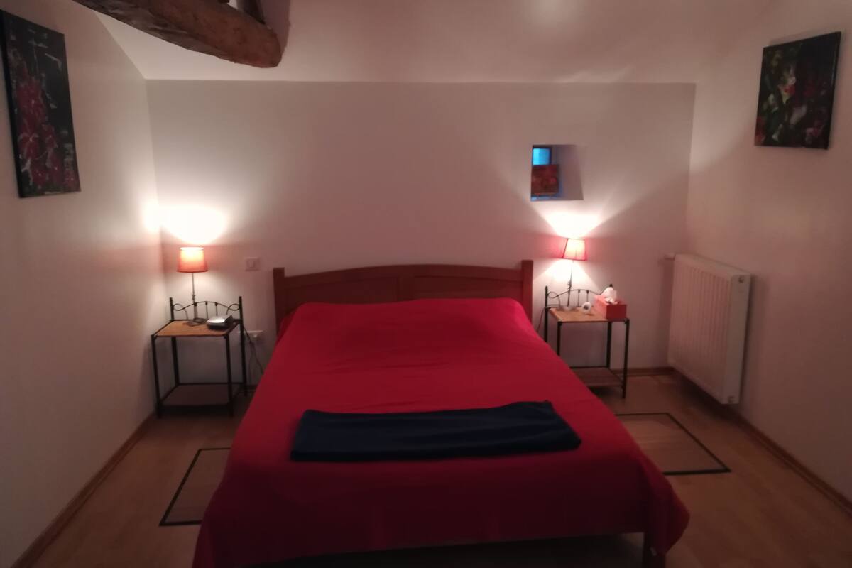 Um quarto pequeno e aconchegante com uma cama de solteiro, duas mesas de cabeceira e um radiador. Há duas luminárias fixadas na parede.