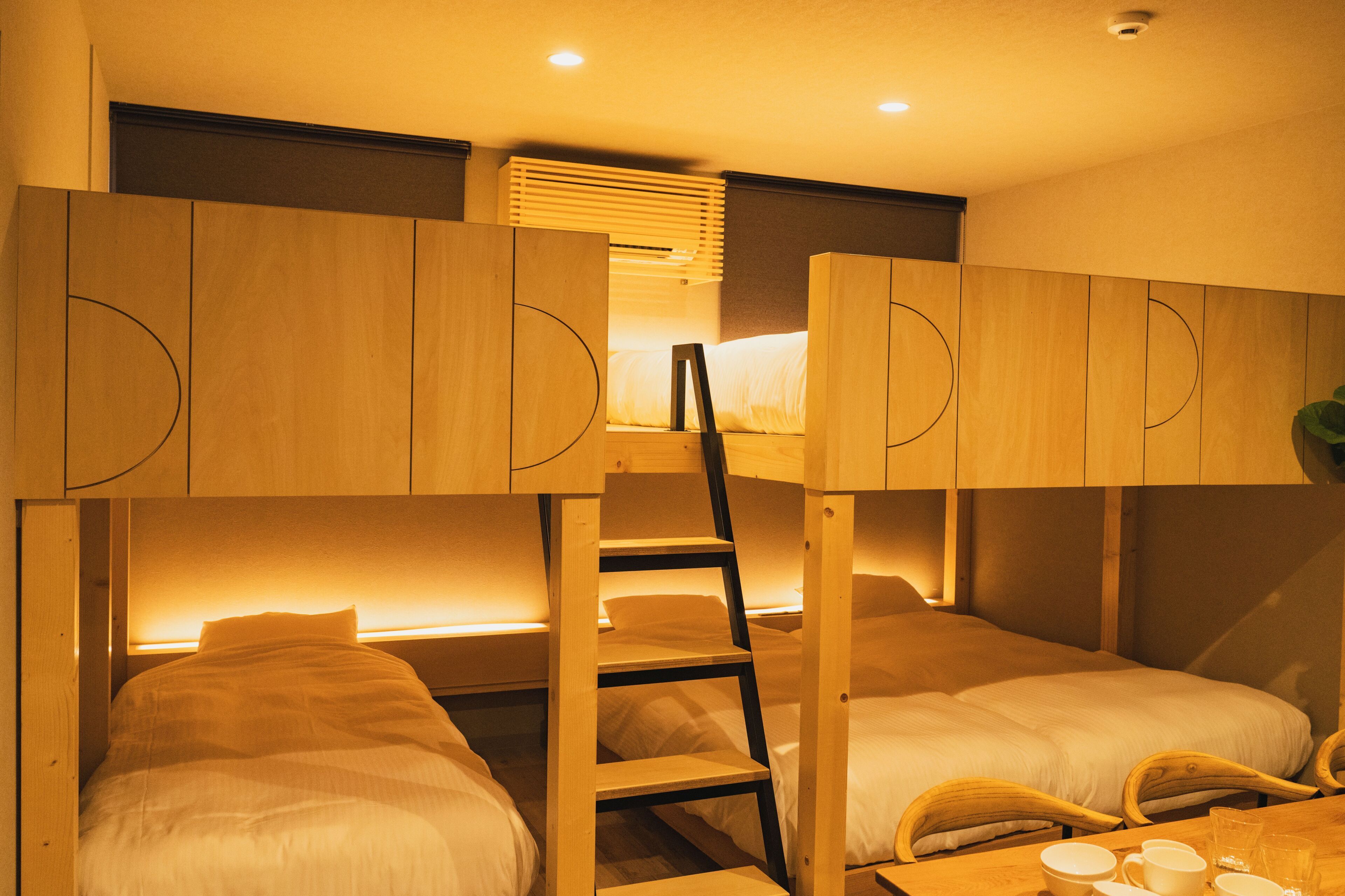 Quarto tipo dormitório com beliches, uma escada e uma mesa com copos e copos.