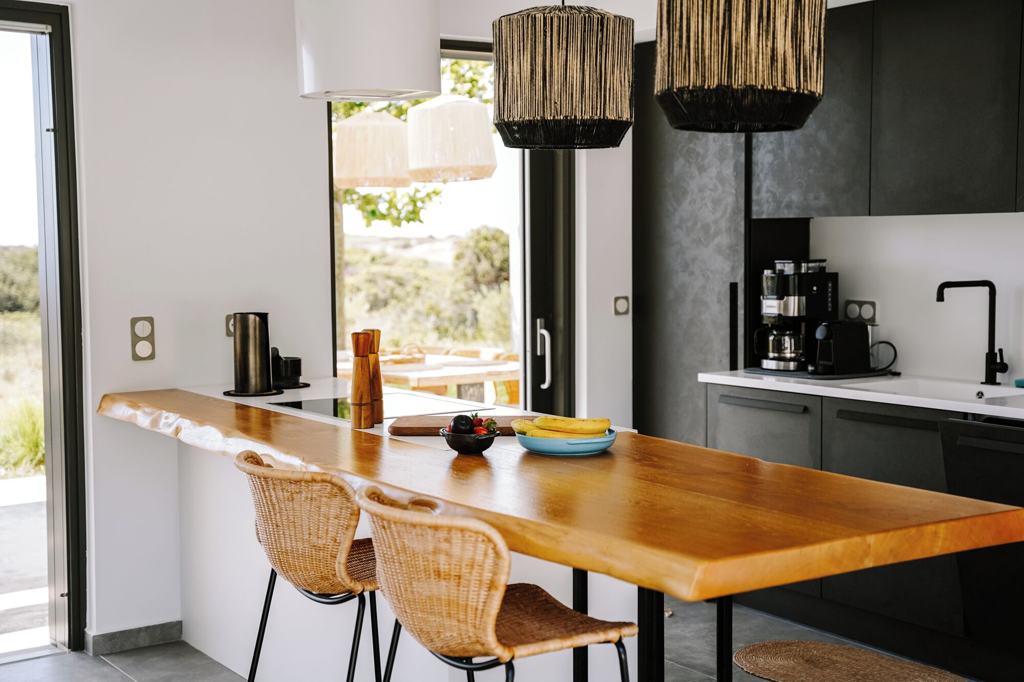 Uma cozinha moderna com mesa de madeira, cadeiras de vime e máquina de café.