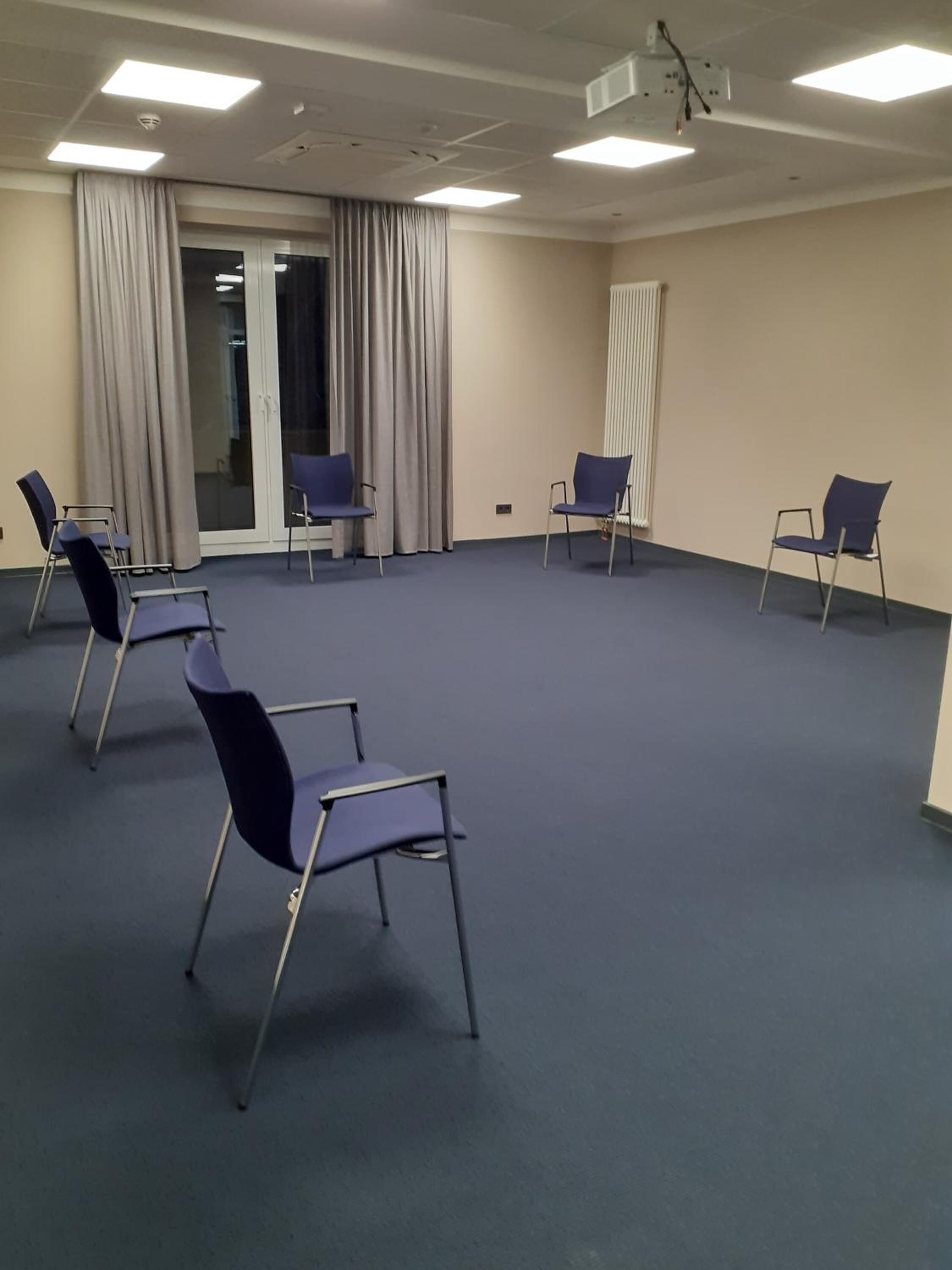 Uma sala de conferências com uma mesa grande, quatro cadeiras, um projetor e uma janela com cortinas.