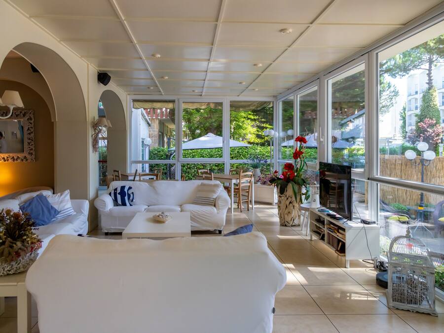 Ampla sala de estar com uma grande janela, um sofá branco, uma televisão e uma mesa de jantar.