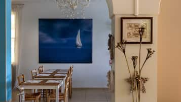 Uma área de refeições com uma mesa posta para quatro pessoas, um candelabro, um quadro na parede e um arranjo de plantas decorativo.