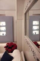 Quarto de hotel com um espelho grande, um sofá branco e um vaso de flores vermelhas.