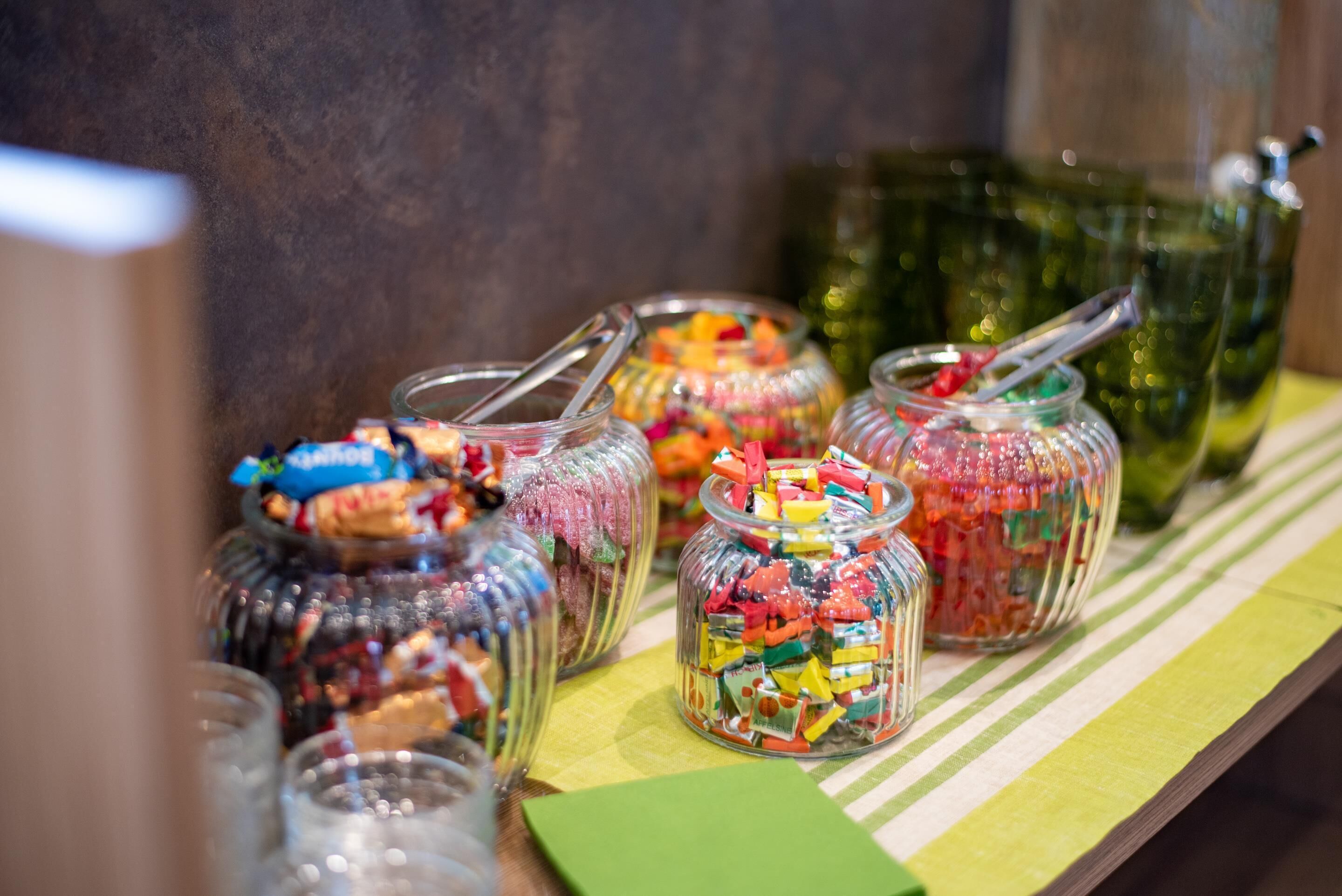 Diversos doces coloridos em potes de vidro sobre uma mesa.