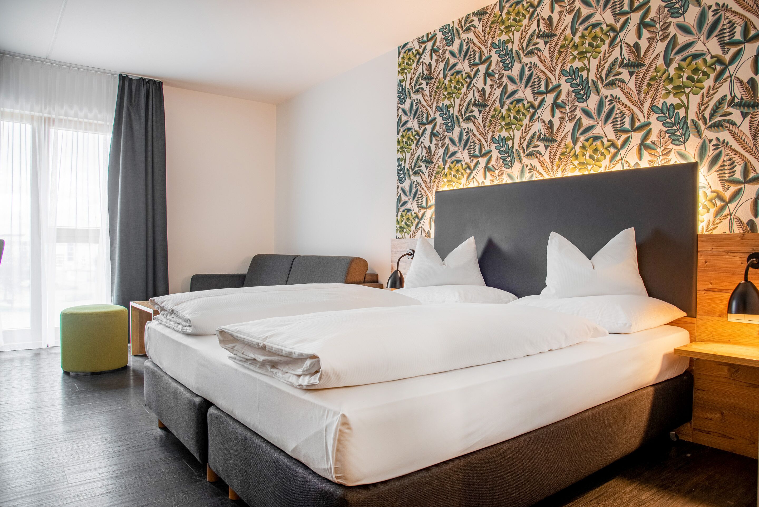 Quarto de hotel moderno com uma cama grande, um espaço de estar pequeno e uma parede estampada.