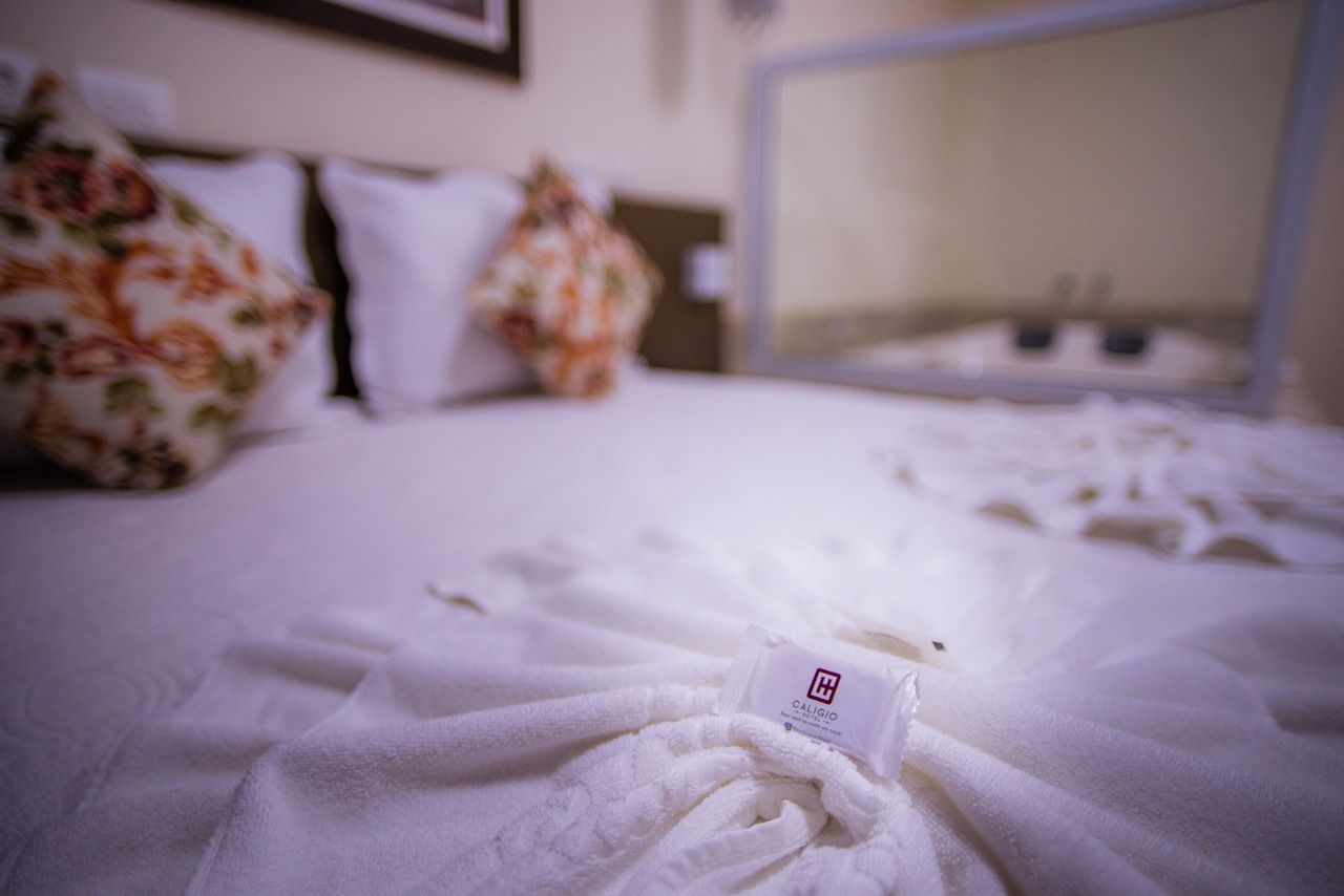 Quarto de hotel com cama bem arrumada, etiqueta visível no cobre-leito e um espelho grande na parede.