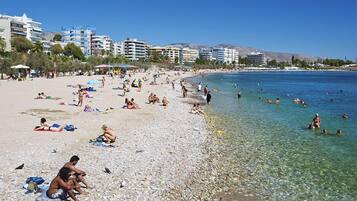 Uma praia com pessoas tomando sol e nadando, cercada por edifícios.