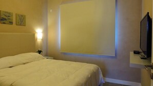 Quarto de hotel com cama, televisão de tela plana e luminária de parede.