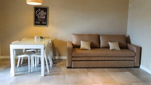 Uma sala de estar com um sofá bege, uma mesa de jantar branca com cadeiras e um lustre.