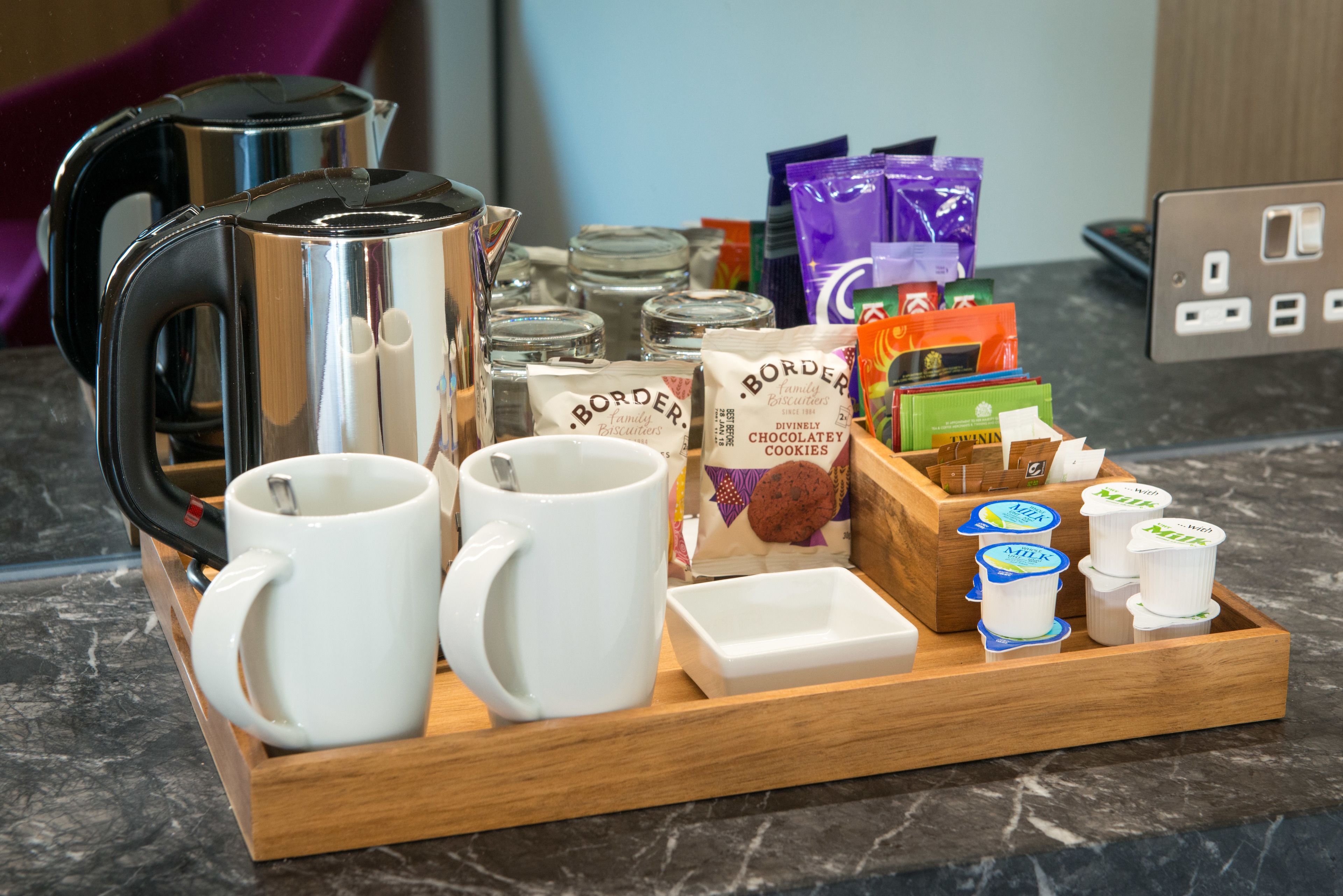 Uma bandeja com chávenas de café, chaleira, frascos e snacks embalados.