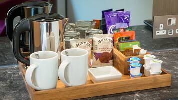 Uma bandeja com chávenas de café, chaleira, frascos e snacks embalados.