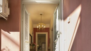 Uma escadaria leva a um corredor com um candelabro, uma porta e uma pequena mesa com uma tigela nos degraus.
